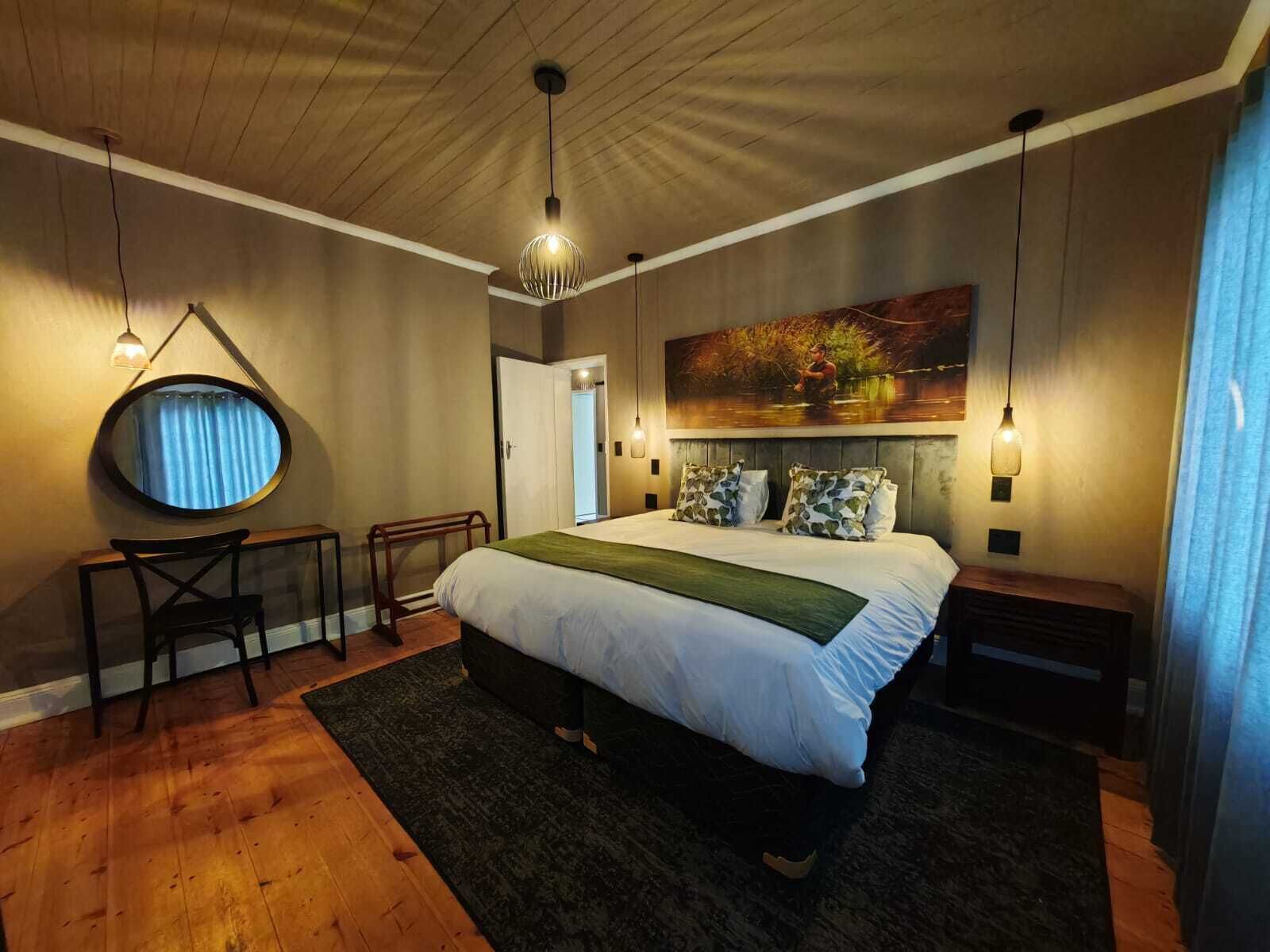 Quarto com uma cama grande, um espelho redondo, uma escrivaninha e um quadro na parede.
