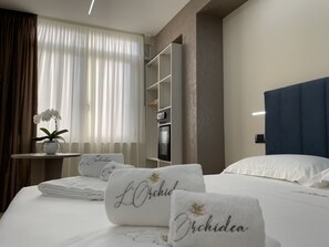 Quarto de hotel com uma cama, mesa de cabeceira com uma orquídea em vaso, guarda-roupa e forno embutido.