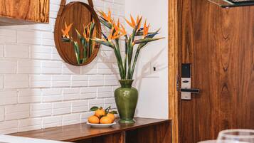 Uma bancada de cozinha com um vaso verde contendo flores laranjas, um prato com laranjas e um armário de madeira.