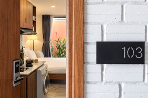 Quarto de hotel com cama, máquina de lavar roupa, área de cozinha e placa com número na parede.