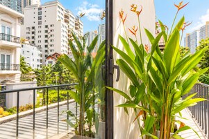 Varanda com plantas em vasos e porta de vidro, com vista para um horizonte urbano com edifícios altos.