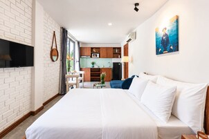 Quarto de hotel com uma cama grande, televisão fixada na parede, área de cozinha e um quadro na parede.