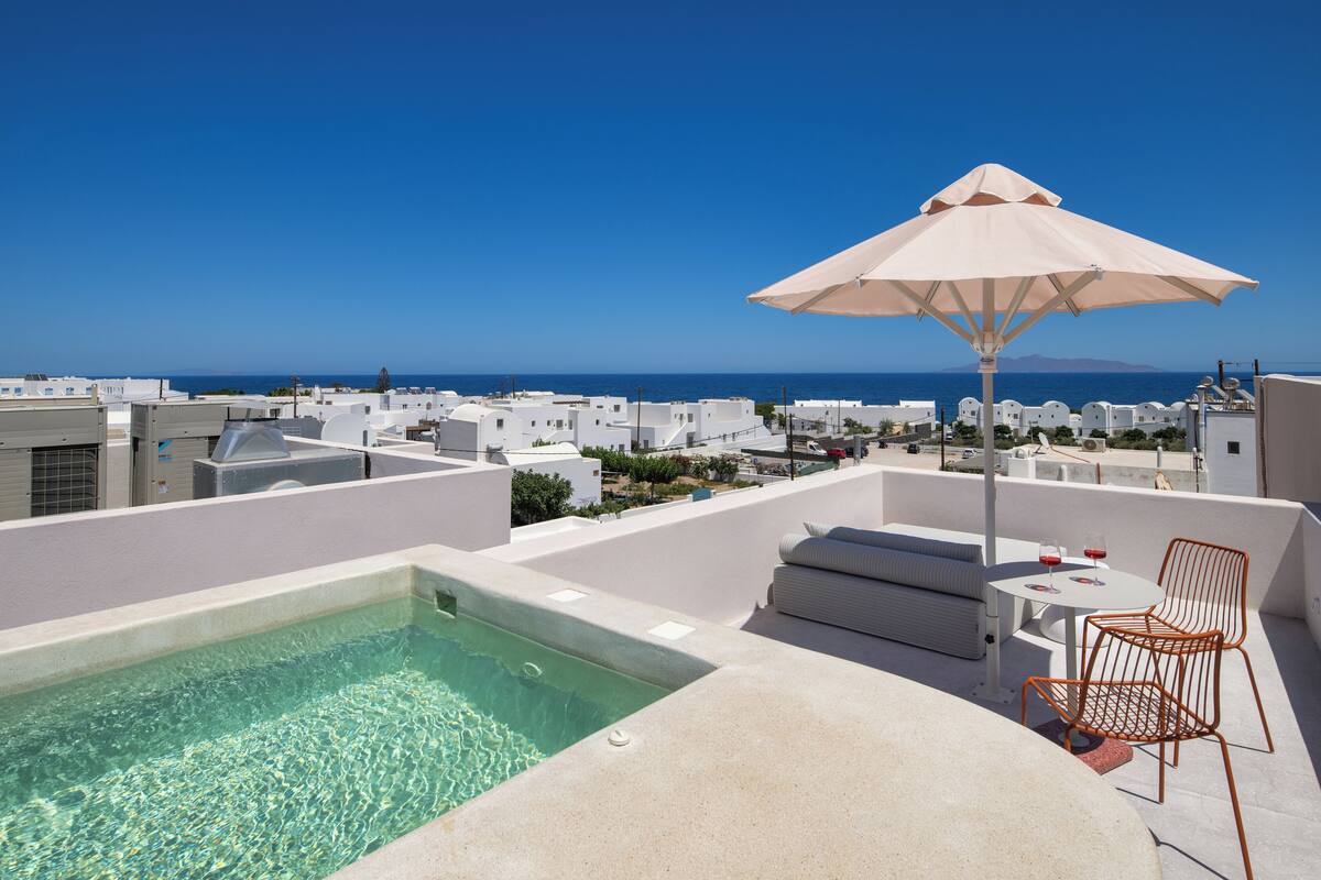 Uma piscina no terraço com água cristalina, edifícios brancos e vista para o mar.
