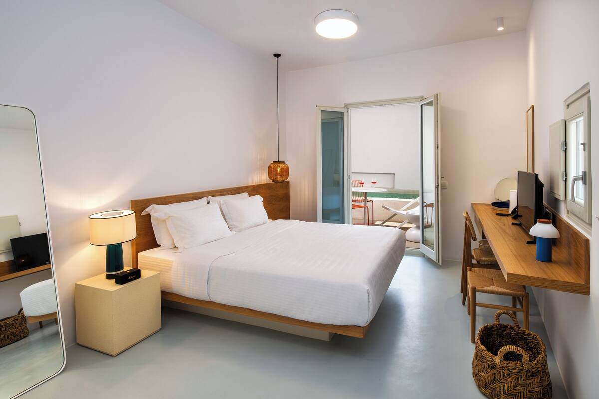Quarto de hotel moderno com cama, mesa de cabeceira, abajur e escrivaninha com cadeira.