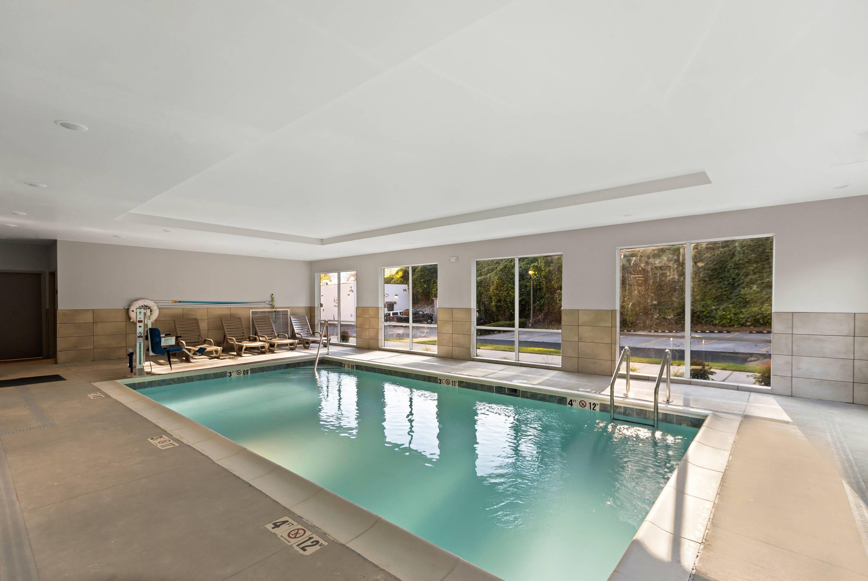 Piscina interior com água cristalina, cadeira de salva-vidas e escada para piscina.