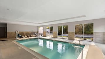 Piscina interior com água cristalina, cadeira de salva-vidas e escada para piscina.