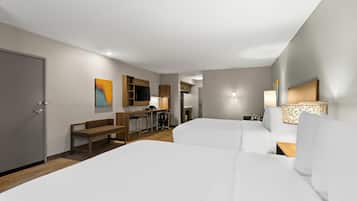 Quarto de hotel com duas camas, uma escrivaninha, uma cadeira, um banco, uma televisão e um abajur.