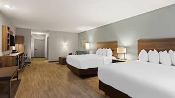 Quarto de hotel com duas camas, uma escrivaninha, uma cadeira, um abajur e uma televisão.