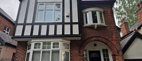 Uma casa em estilo Tudor com dois andares, fachada preta e branca, detalhes em tijolo e janela saliente.