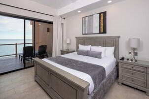 Quarto com uma cama grande, uma mesa de cabeceira, uma cadeira e vista para o mar.