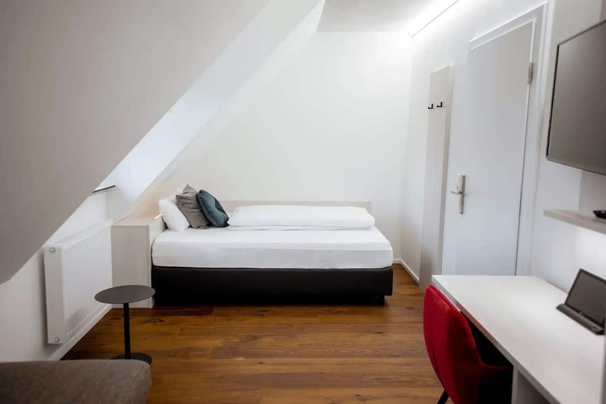 Um quarto pequeno e moderno com uma cama, uma escrivaninha e uma cadeira.