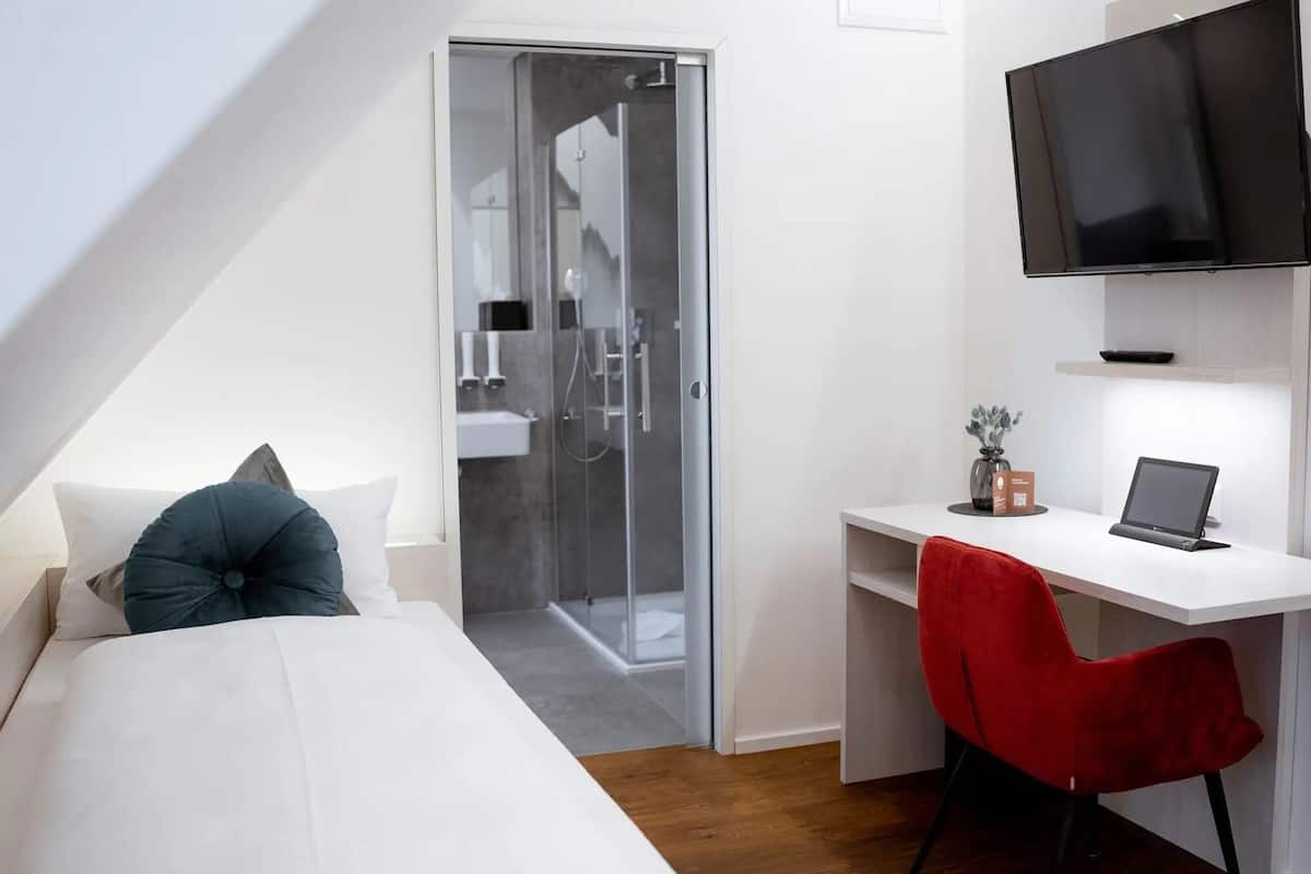 Quarto com cama, escrivaninha com laptop, televisão e chuveiro.
