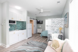 Um espaço compacto com cozinha compacta, cama, televisão e ventoinha de teto.
