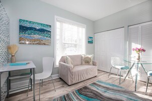 Uma sala de estar moderna com um sofá, cadeiras, uma mesa de vidro, uma janela grande e um elemento decorativo na parede.