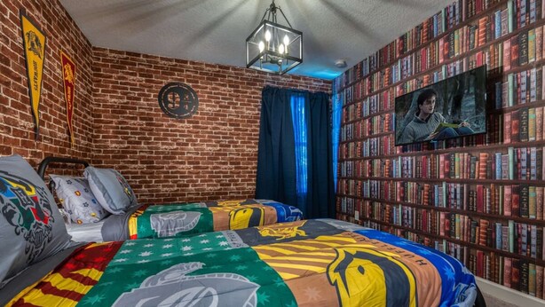 Quarto com duas camas, parede de tijolos, estante e televisão.