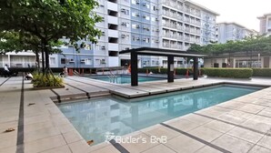 Piscina com área coberta, cercada por um edifício com várias varandas e aparelhos de ar condicionado.
