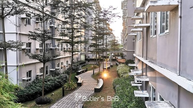 Edifício residencial com várias varandas, um caminho central e vegetação ao redor.