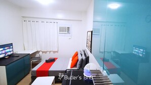 Quarto de hotel com uma cama, uma escrivaninha com computador, televisão e ar condicionado.