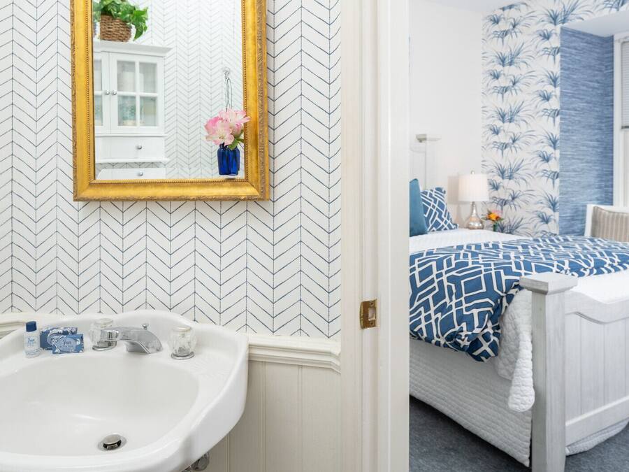 Casa de banho com uma pia branca, um espelho com moldura dourada e papel de parede estampado.