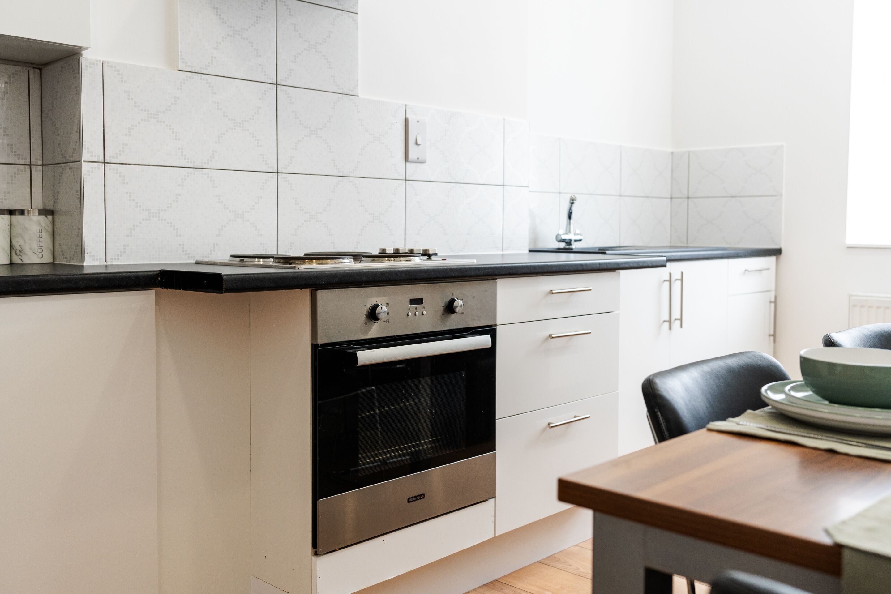 Uma cozinha moderna com armários brancos, bancada preta e eletrodomésticos de aço inoxidável.