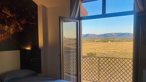 Quarto com uma grande janela que oferece vista para um campo e montanhas ao longe.