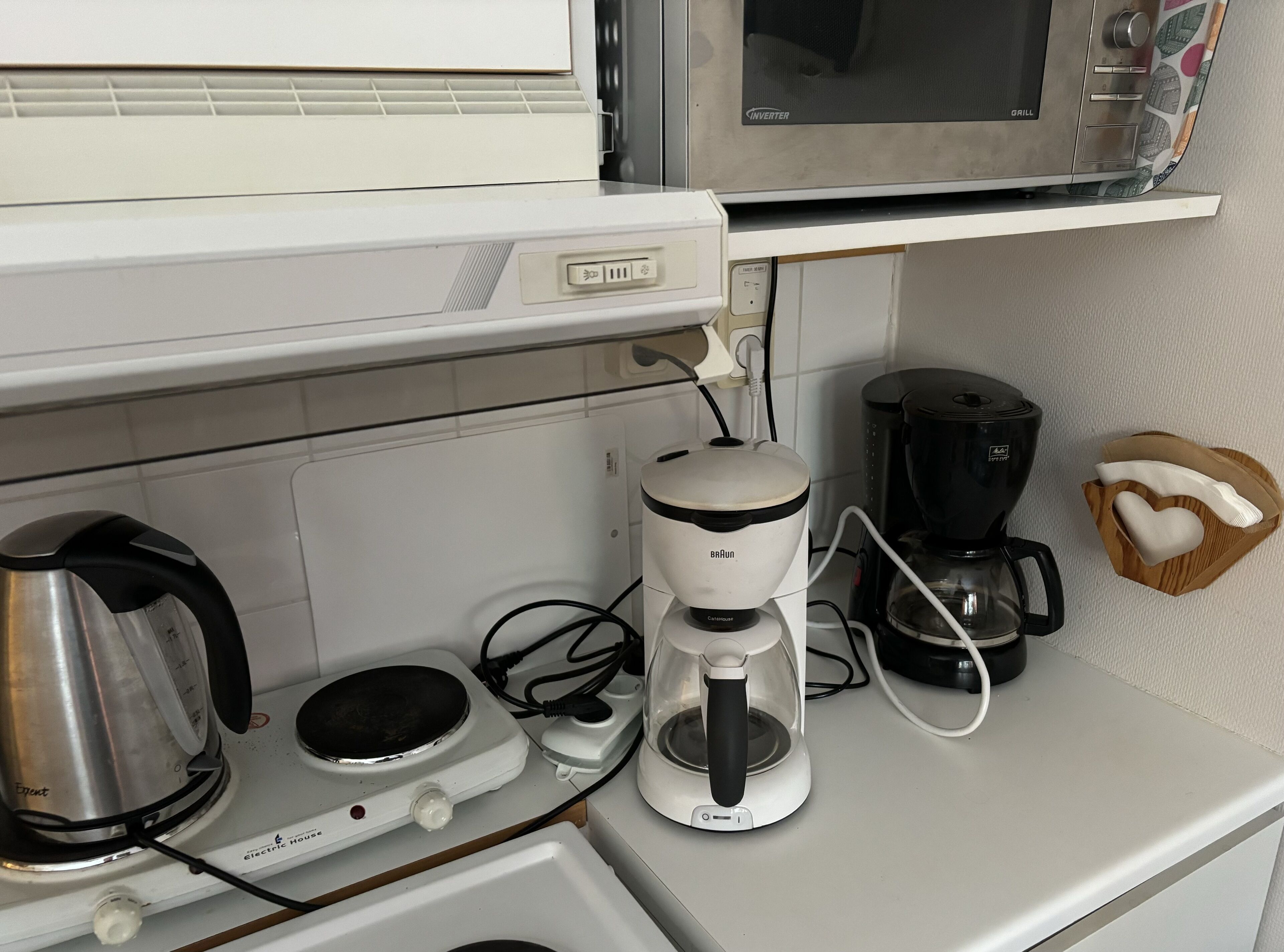 Uma cozinha com micro-ondas, chaleira elétrica, máquina de café e chaleira no balcão.