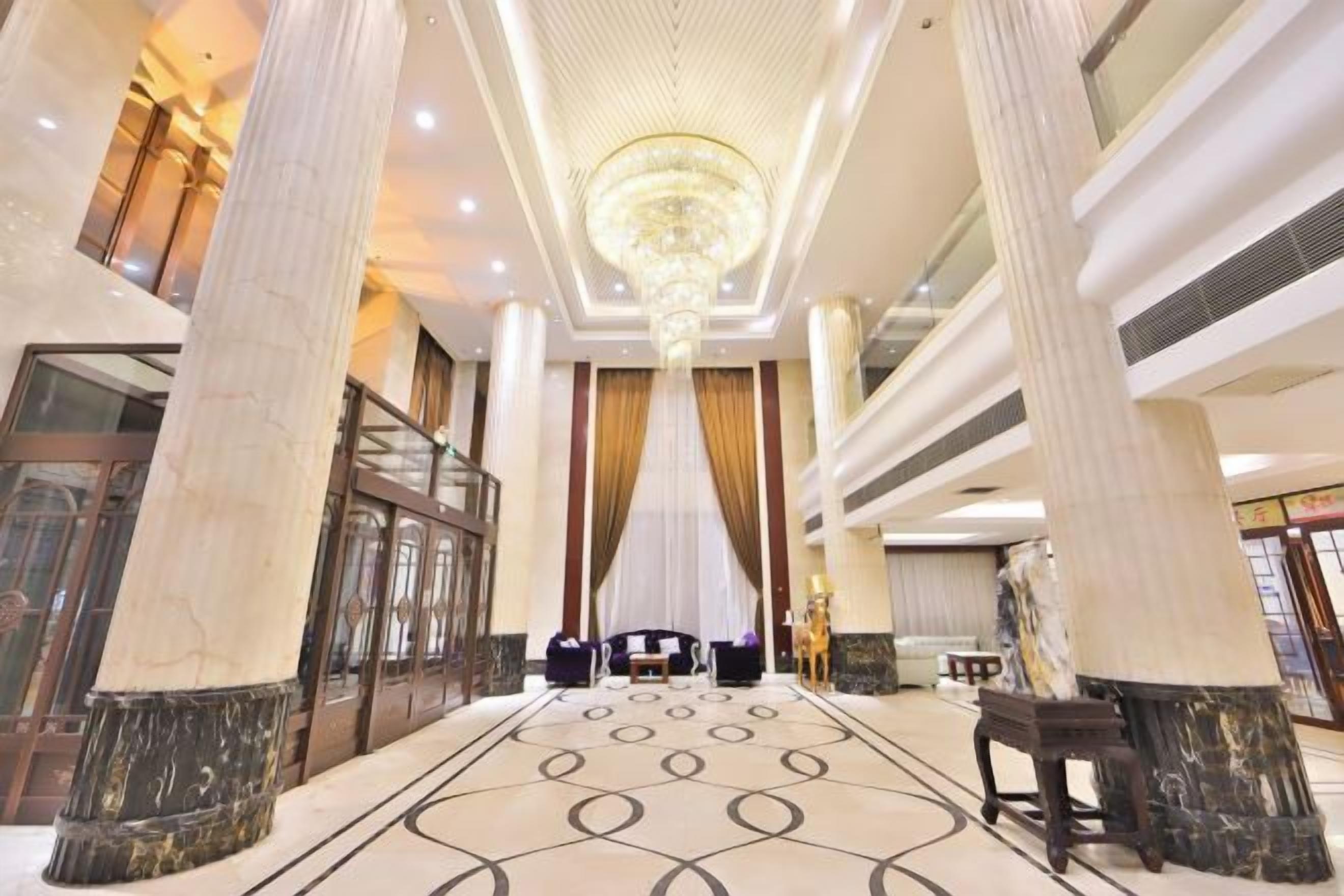 Um hall imponente com colunas de mármore, piso estampado e um lustre grande.