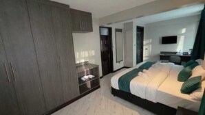 Quarto de hotel moderno com uma cama grande, um guarda-roupa, uma escrivaninha e uma televisão.