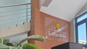 Um hall de hotel com uma planta em vaso, um púlpito e uma placa com a inscrição 'Hotel Lourdes'.