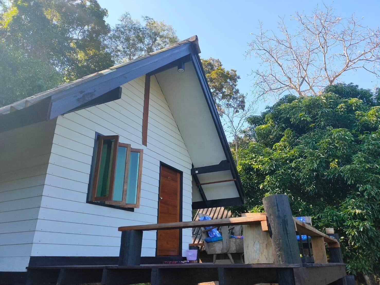 Uma cabana branca com telhado inclinado, porta de madeira e janela com persianas verdes.