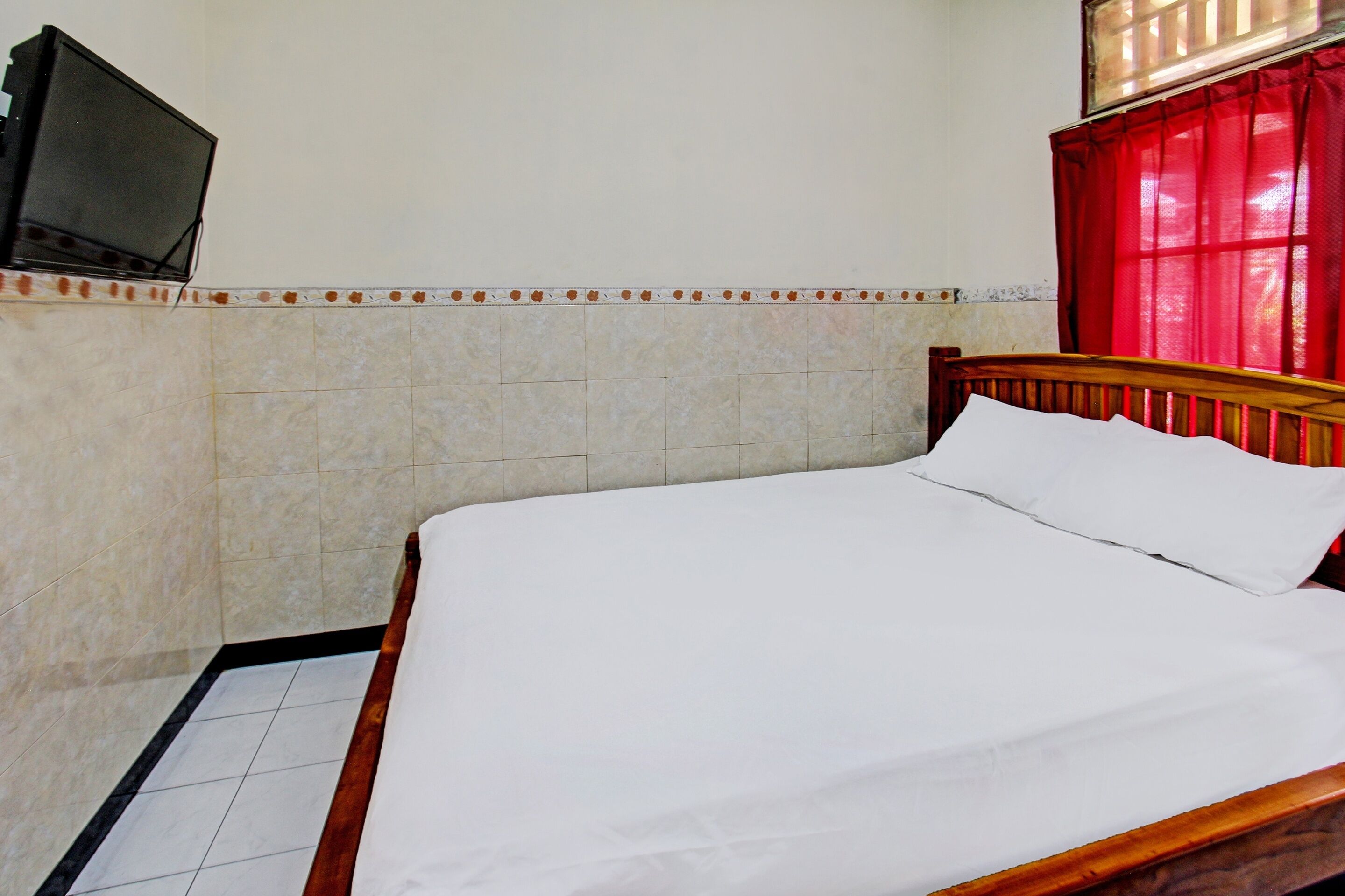 Cama de casal com roupa de cama branca num quarto com paredes em azulejo e cabeceira de madeira.