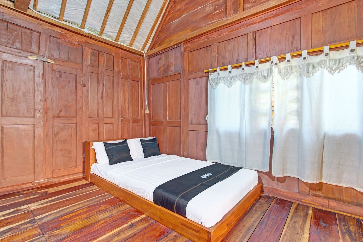Quarto com paredes de madeira, uma cama, cortinas e piso de madeira.