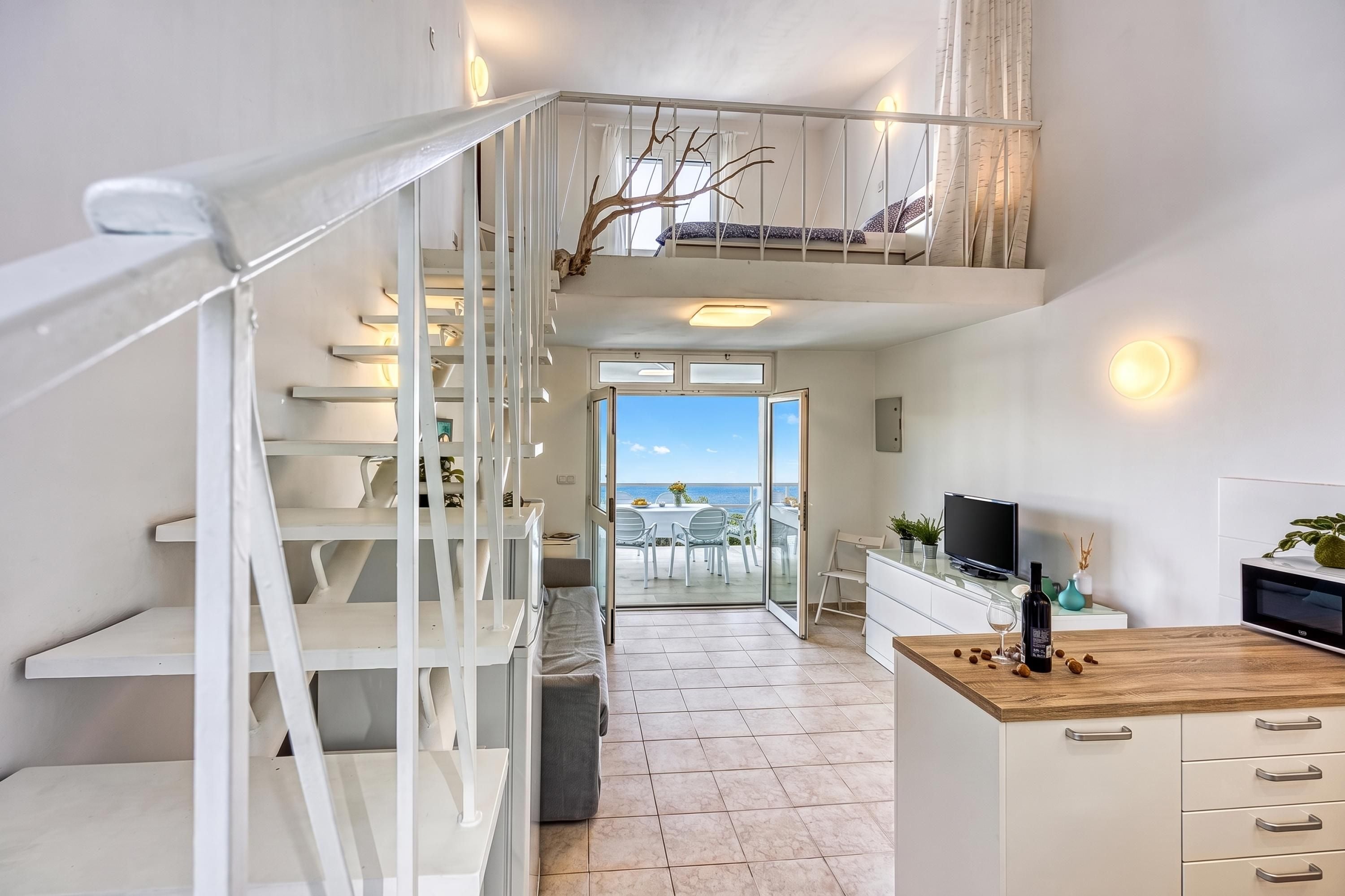 Interior moderno com escada que leva a uma varanda com vista para o mar.