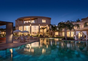 Um resort moderno com uma piscina grande, espreguiçadeiras e um edifício bem iluminado.