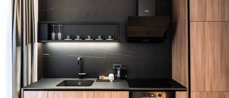 Uma cozinha moderna com bancada preta, armários de madeira, forno embutido e cafeteira.