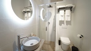 Uma casa de banho moderna com um espelho redondo, uma pia, uma sanita e um chuveiro com parede de vidro.