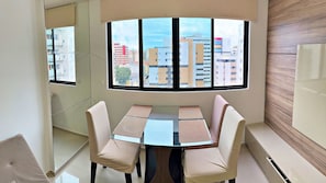 Quarto moderno com mesa de vidro, quatro cadeiras e uma grande janela com vista para a cidade.