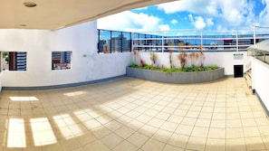Amplo espaço interno com piso de azulejos, janelas grandes e vista para a paisagem urbana.