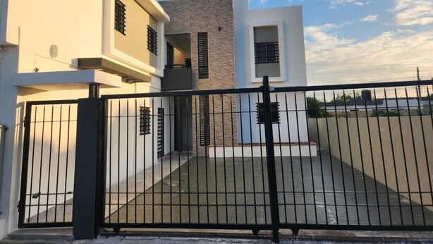 Uma casa moderna de dois andares, com entrada por portão, varanda coberta e ampla vista do céu.