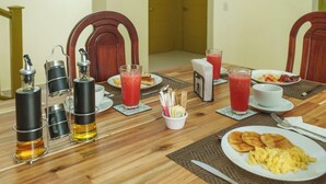 Mesa de café da manhã posta com ovos mexidos, panquecas e torradas, além de duas taças de suco vermelho e uma cafeteira.