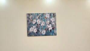 Um sofá preto com três almofadas em um quarto com piso de azulejos e um quadro na parede com flores brancas.