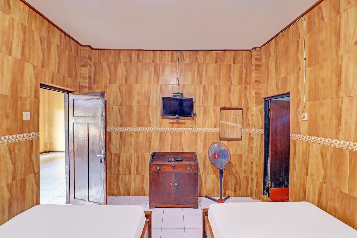 Quarto de hotel com paredes de painel de madeira, televisão na parede, armário de madeira, ventilador e duas camas.