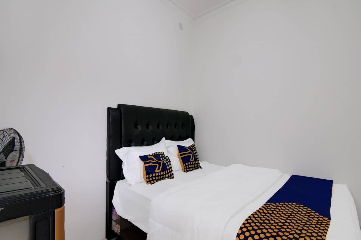 Uma cama com cabeceira preta, roupa de cama branca e duas almofadas decorativas com padrão geométrico.
