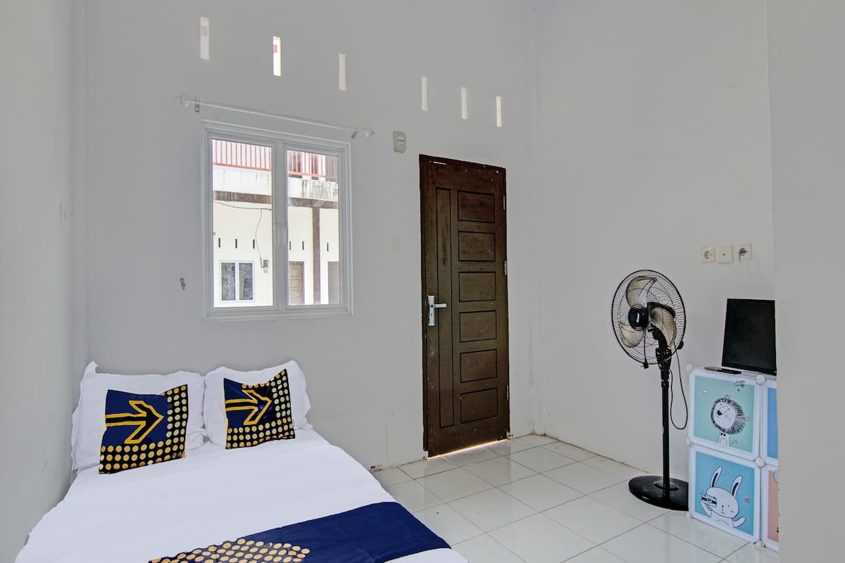 Quarto com cama, janela, porta, ventoinha e um pequeno armário.