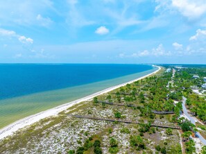 Paisagem costeira com praia, águas azuis cristalinas e um caminho que leva a um conjunto de edifícios.