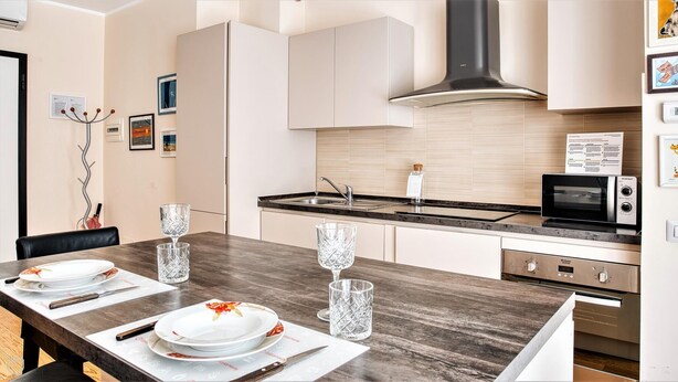 Uma cozinha moderna com bancada escura, eletrodomésticos de aço inoxidável e armários em tons claros.