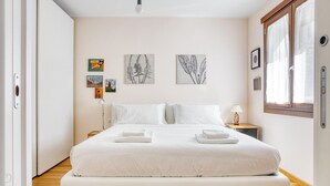 Um quarto com uma cama grande, roupa de cama branca e obras de arte na parede.
