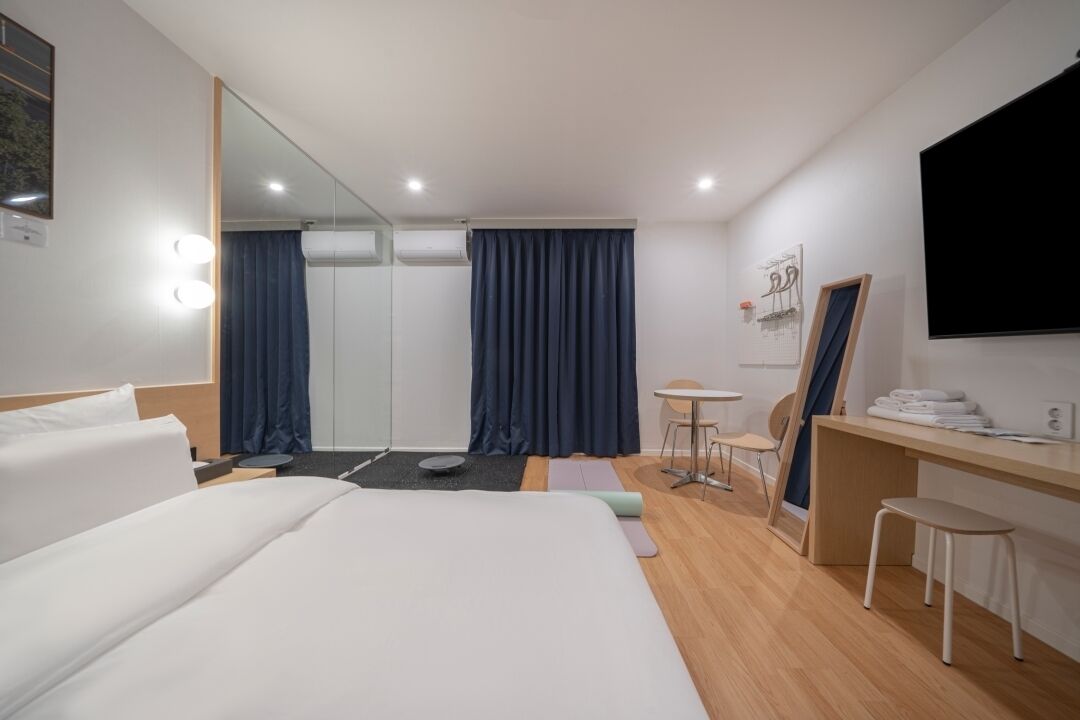 Quarto de hotel com uma cama grande, uma escrivaninha, uma cadeira, uma mesa pequena, um espelho e uma televisão.