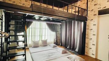 Quarto compacto com beliches, escada, mesa pequena e janela com cortinas.