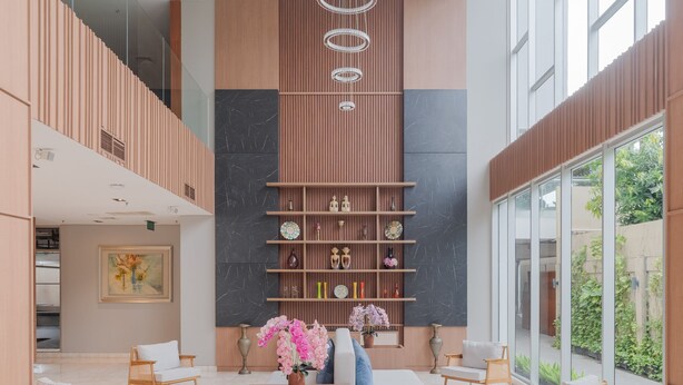 Um hall amplo com área de estar central, prateleira na parede com objetos decorativos e janelas grandes que oferecem vista para o exterior.